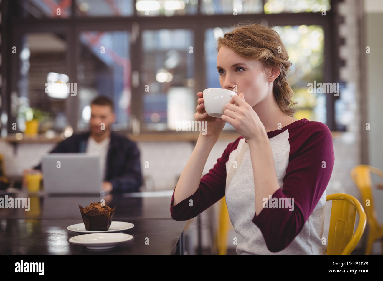 Beautiful young woman drinking coffee from cup while sitting at table ...