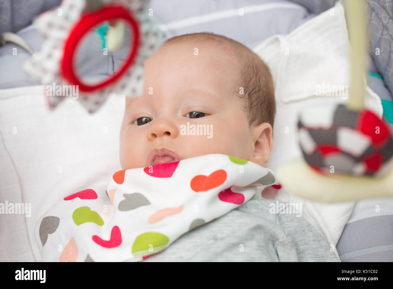 Cute newborn baby girl in a rocking seat with toys hanging above her ...