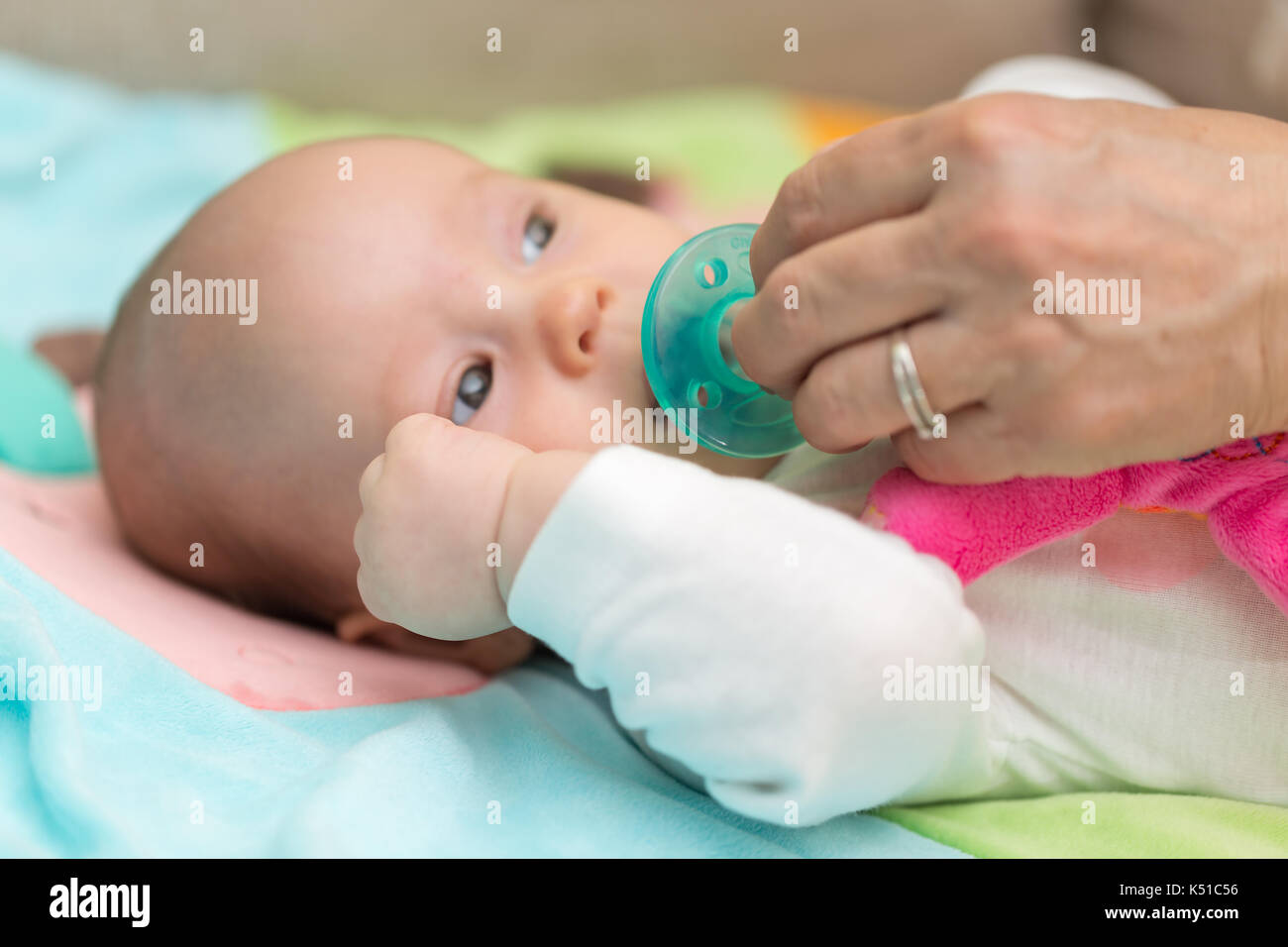 Female hand trying to put a green pacifier into her grandchild's mouth ...