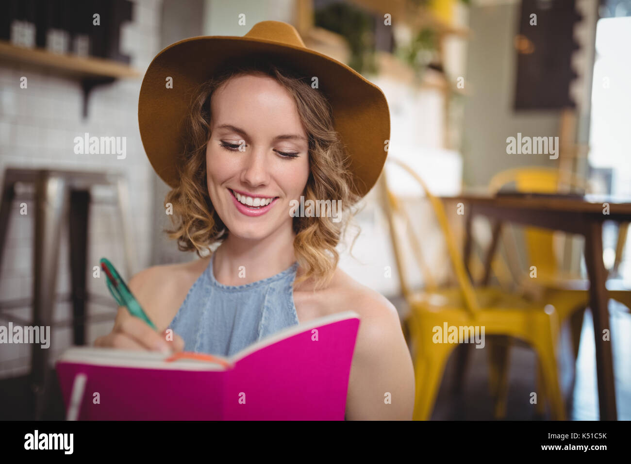 Smiling beautiful young woman writing in pink dairy at coffee shop ...