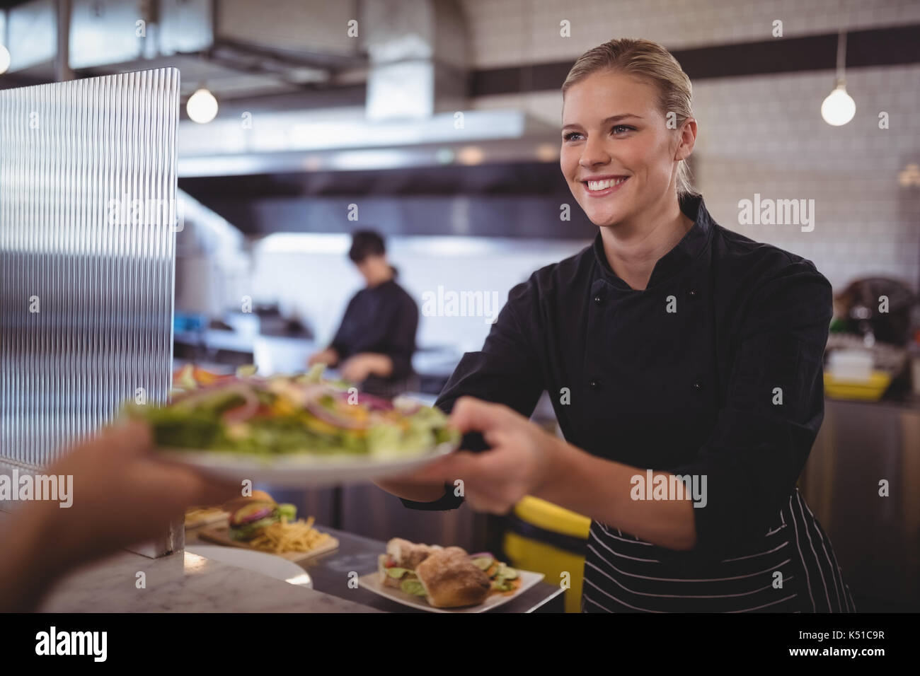 Attractive young female chef giving fresh Greek salad to waiter at ...