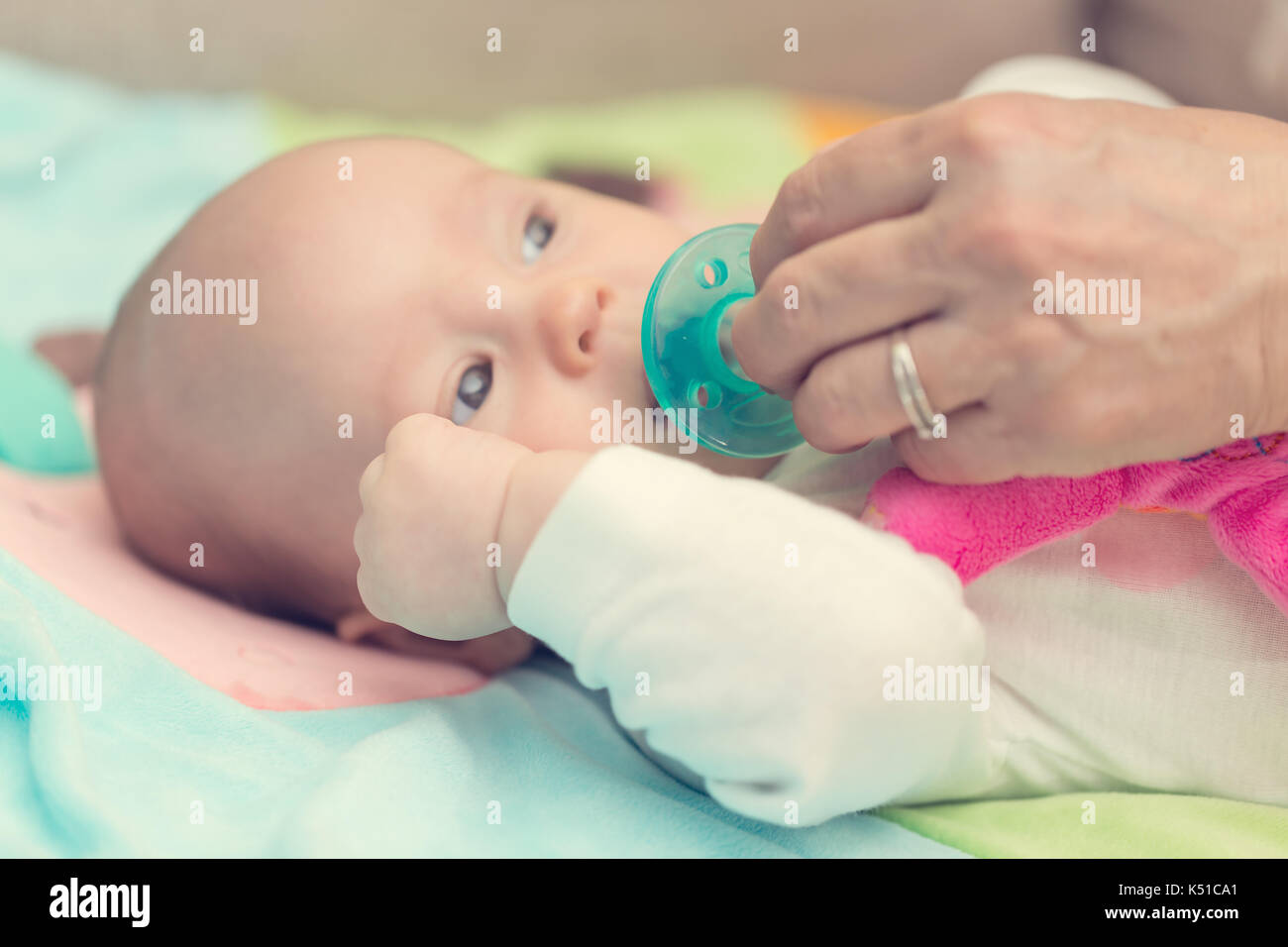 Female hand trying to put a green pacifier into baby girl's mouth ...