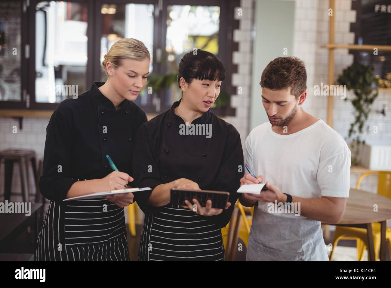 Young waiter and waitress discussing over digital tablet at coffee shop ...