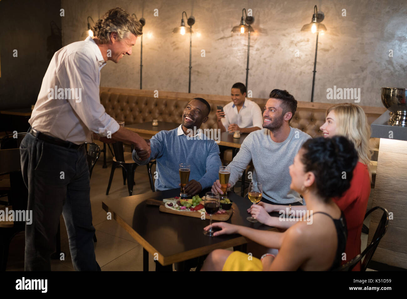 Friends shaking hands while having meal in restaurant Stock Photo - Alamy