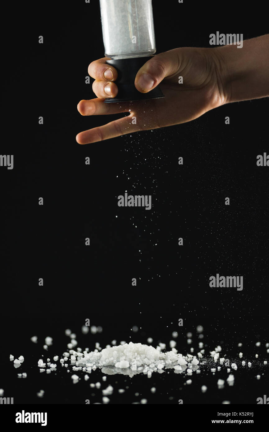 Close-up of mans hand sprinkling sea salt against black background ...
