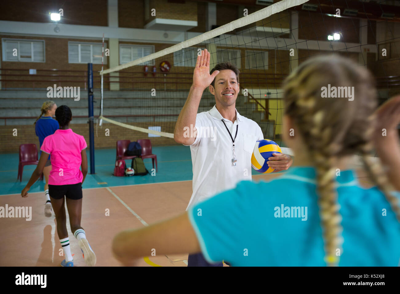 Smiling coach giving high five to female player in volleyball court ...