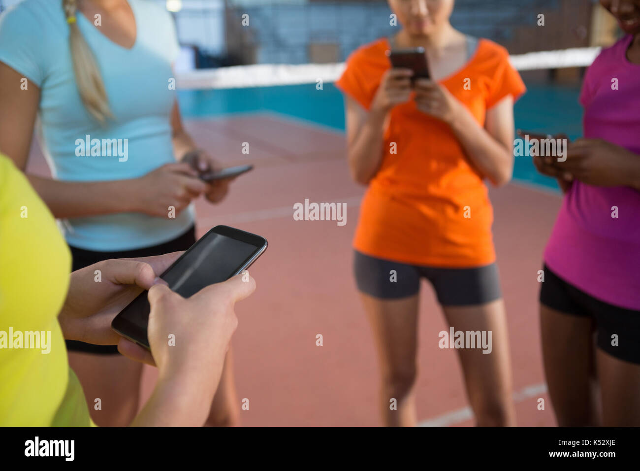 Mid section of female players using mobile phones in volleyball court ...