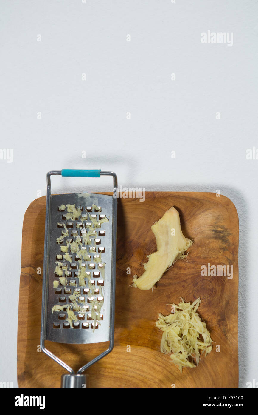 Overhead view of fresh ginger and steel grater on wooden plate over ...