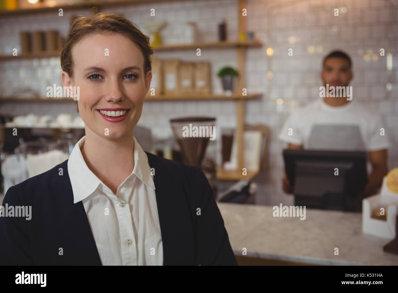 Portrait of smiling female owner with waiter working in background at ...