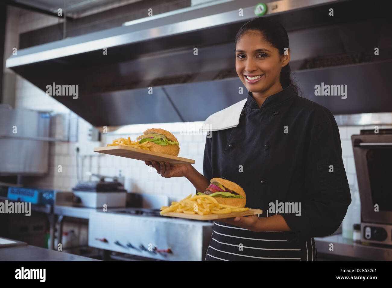 Portrait of smiling waitress with French fries and burger standing in ...