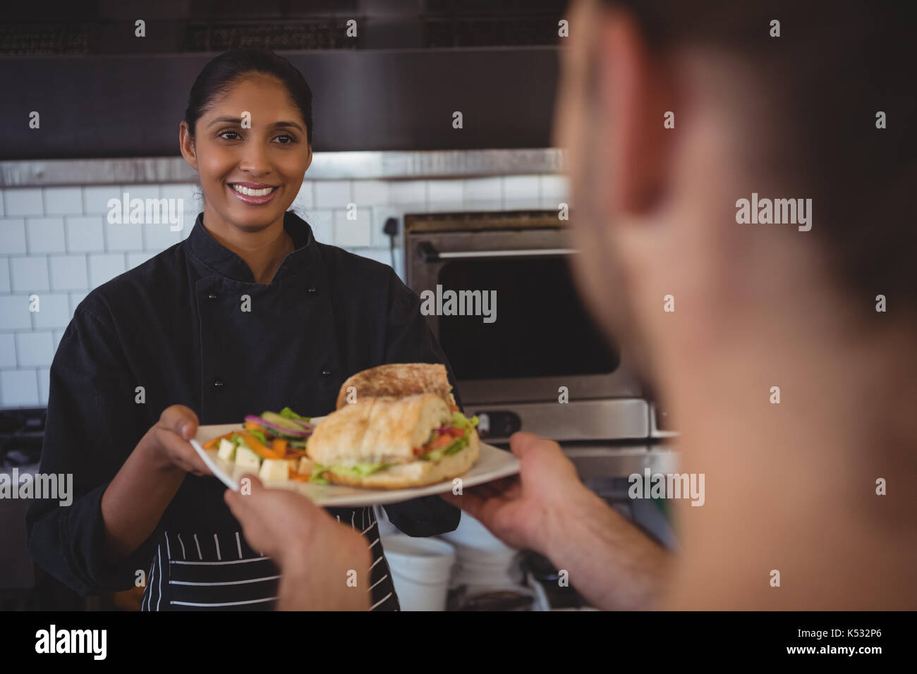 Smiling waitress giving plate with food to coworker while standing at ...