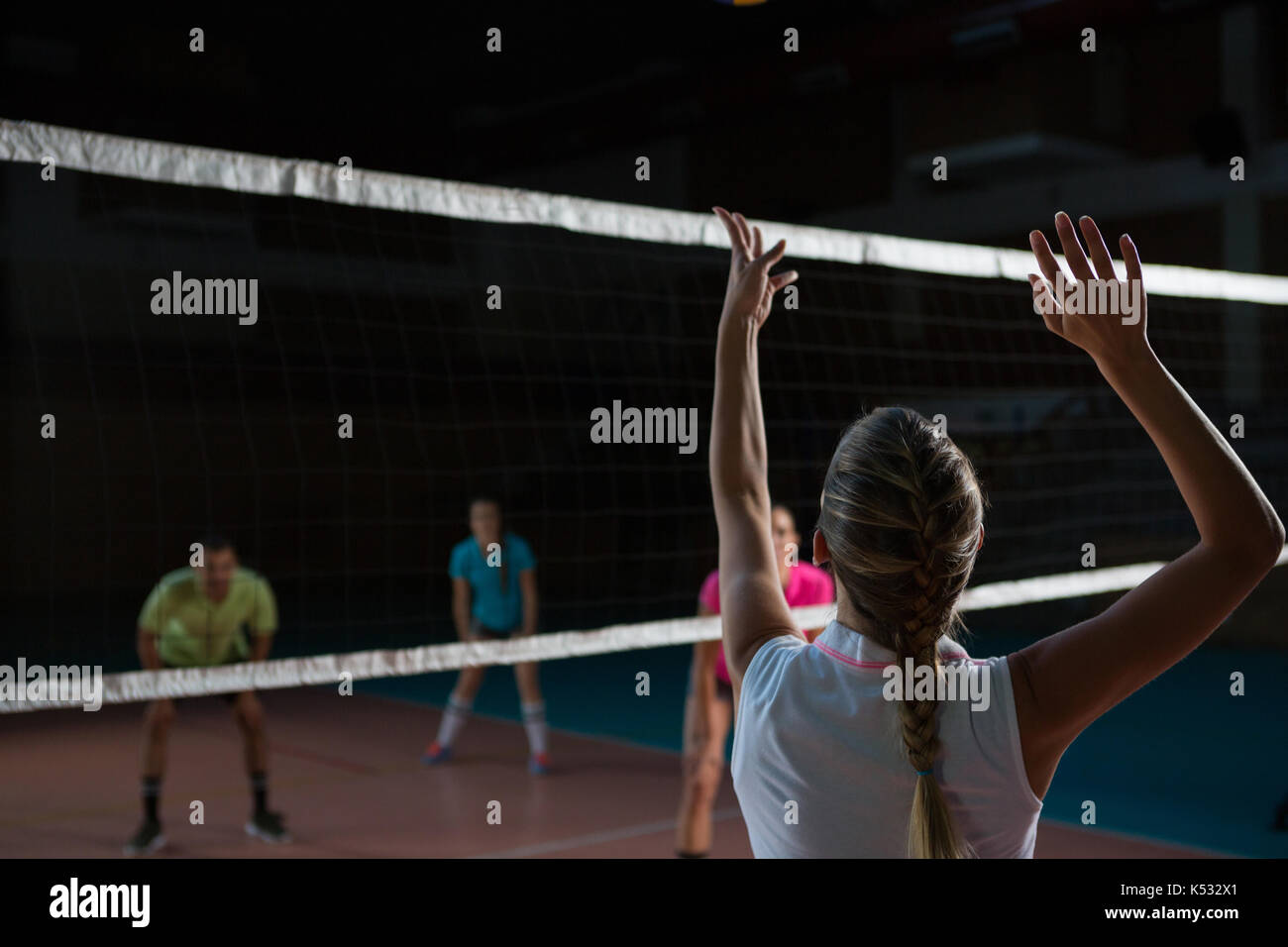 Rear view of female volleyball player with arms raised playing at court ...