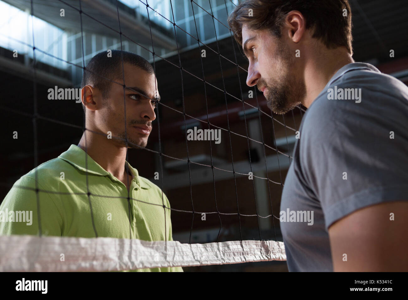 Aggressive male volleyball players looking at each other through net ...