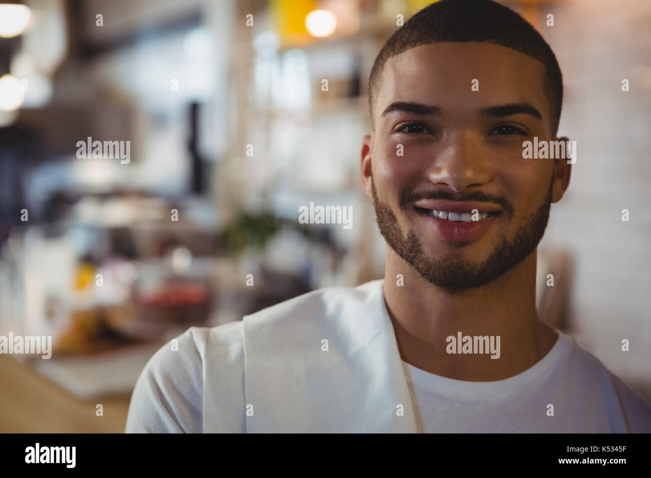 Close-up portrait of smiling young waiter standing in cafe Stock Photo ...