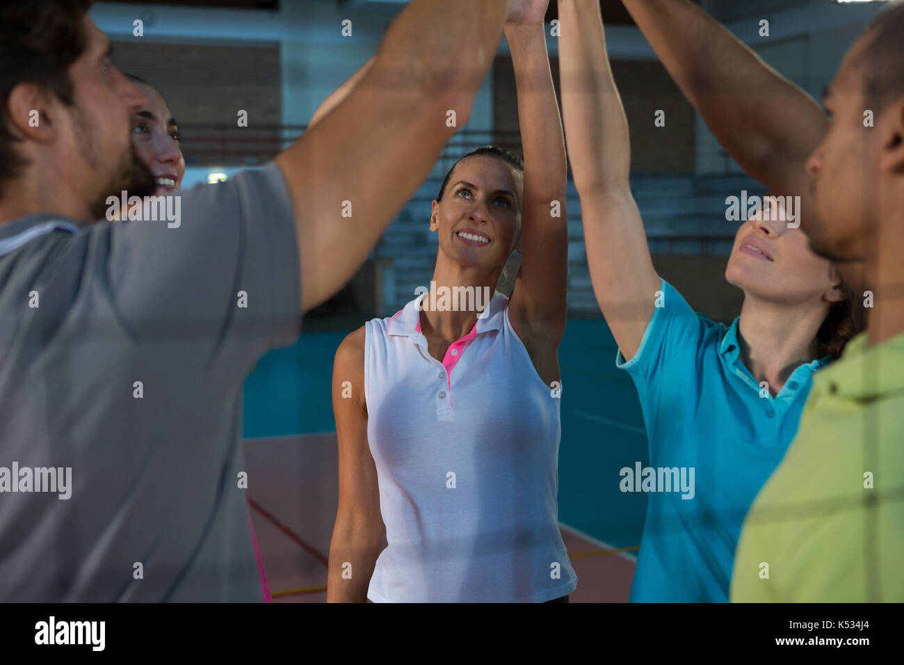Smiling volleyball players giving high-five seen through net at court ...