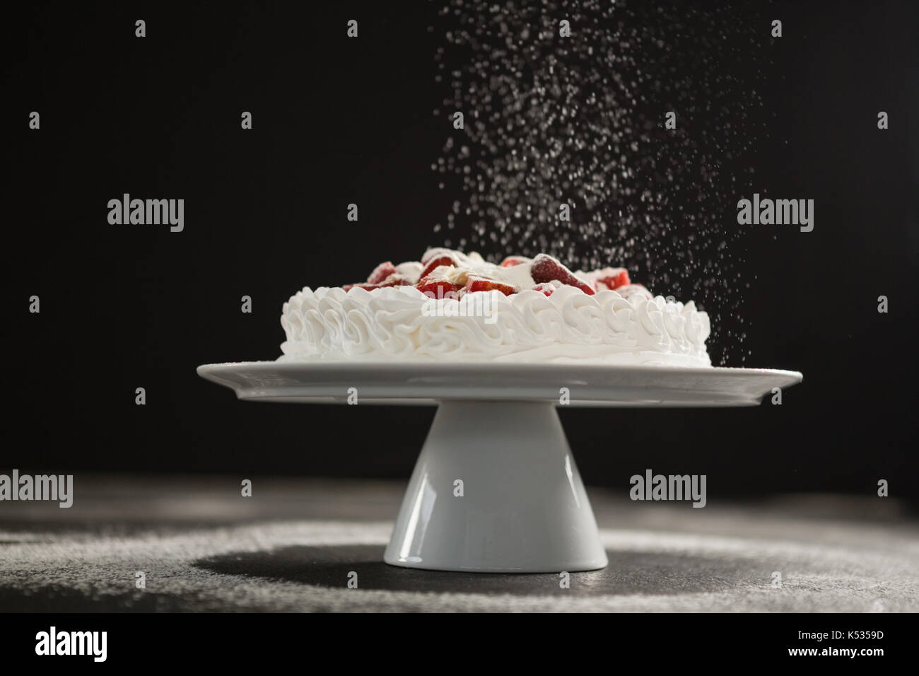 Powdered sugar falling over white cake on stand against black ...