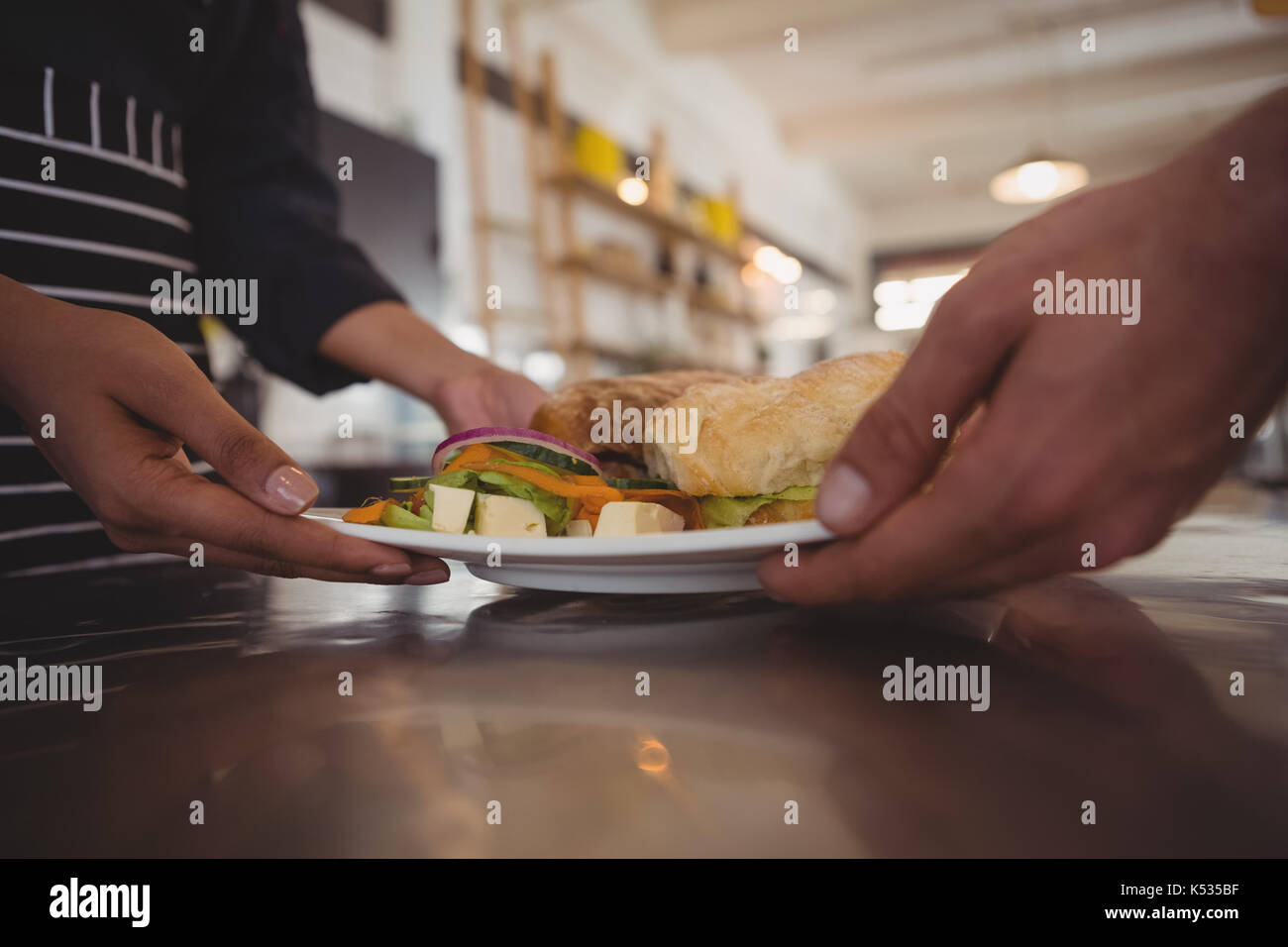 Mid section of waitress giving plate with food to coworker at counter ...