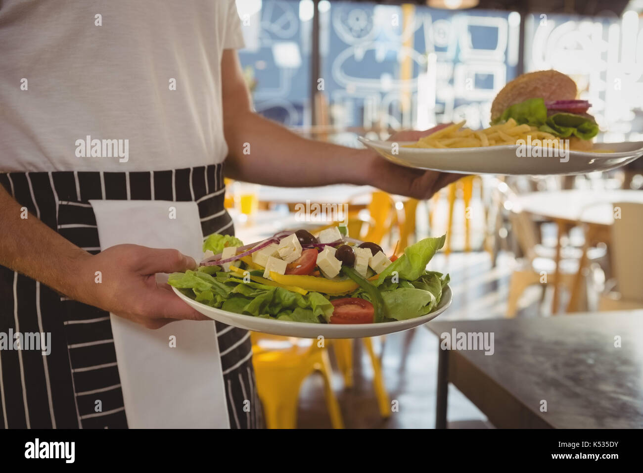 Mid section of waiter serving salad and French fries with burger in ...