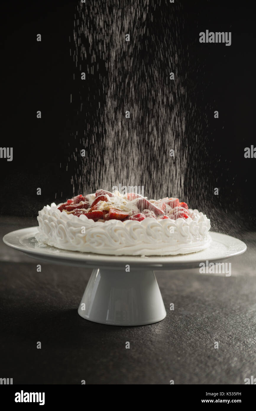 Powdered sugar falling over cake on stand against black background ...