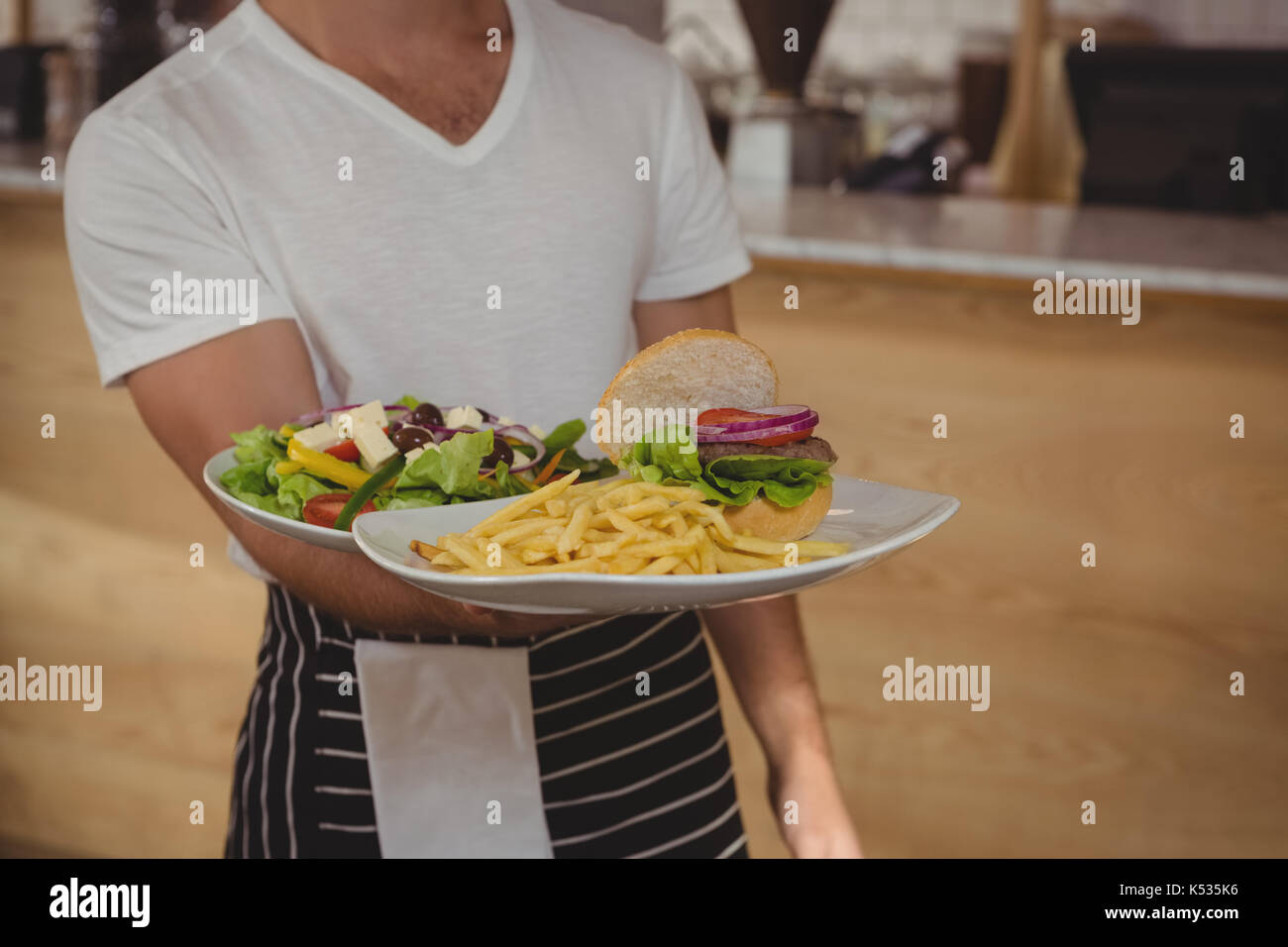 Mid section of waiter holding plate with food while standing by counter ...