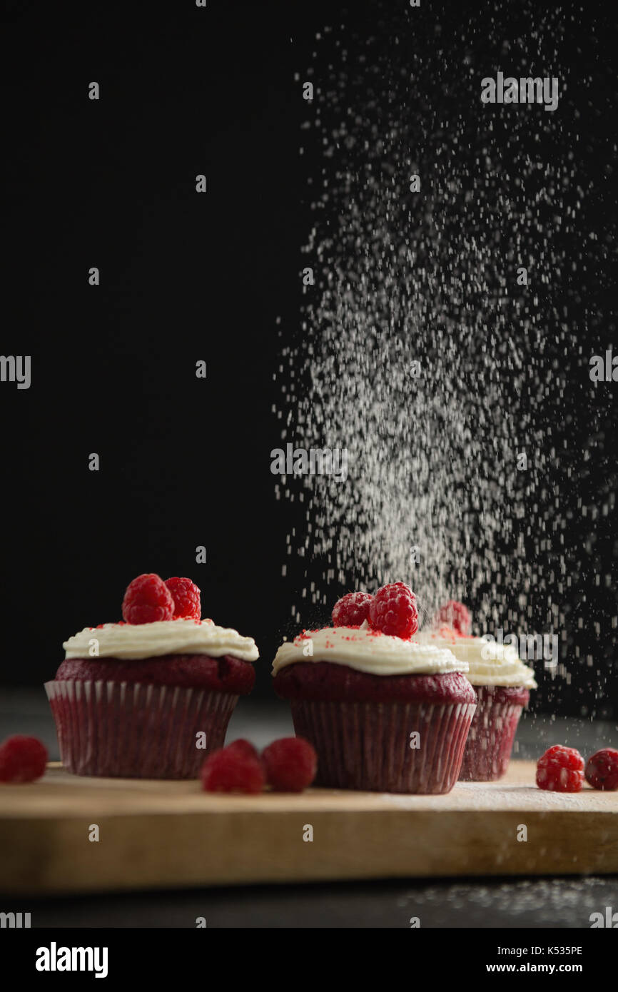 Powdered sugar falling over cupcakes on cutting board against black ...