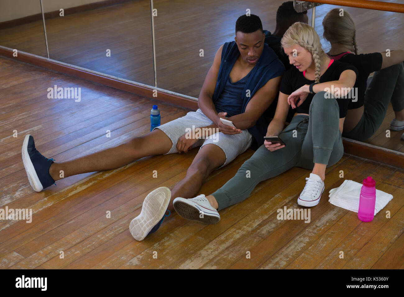 Full length of young dancers using mobile phone on floor in studio ...