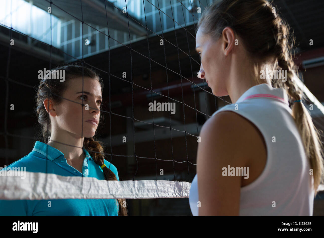 Aggressive female volleyball players looking through net at court Stock ...
