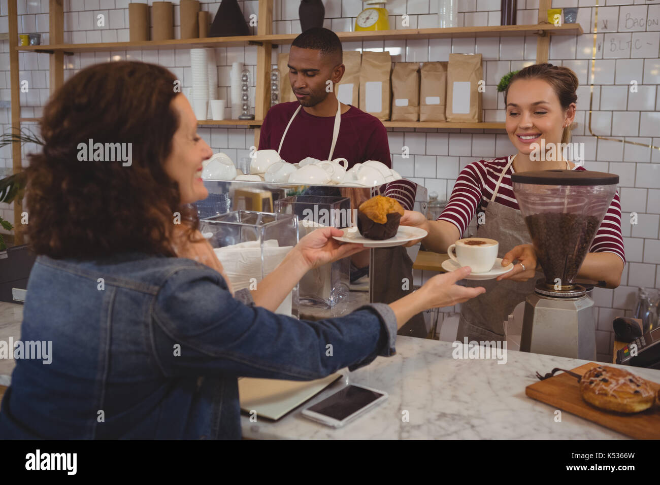 Female owner serving muffin and coffee to customer at cafe Stock Photo ...
