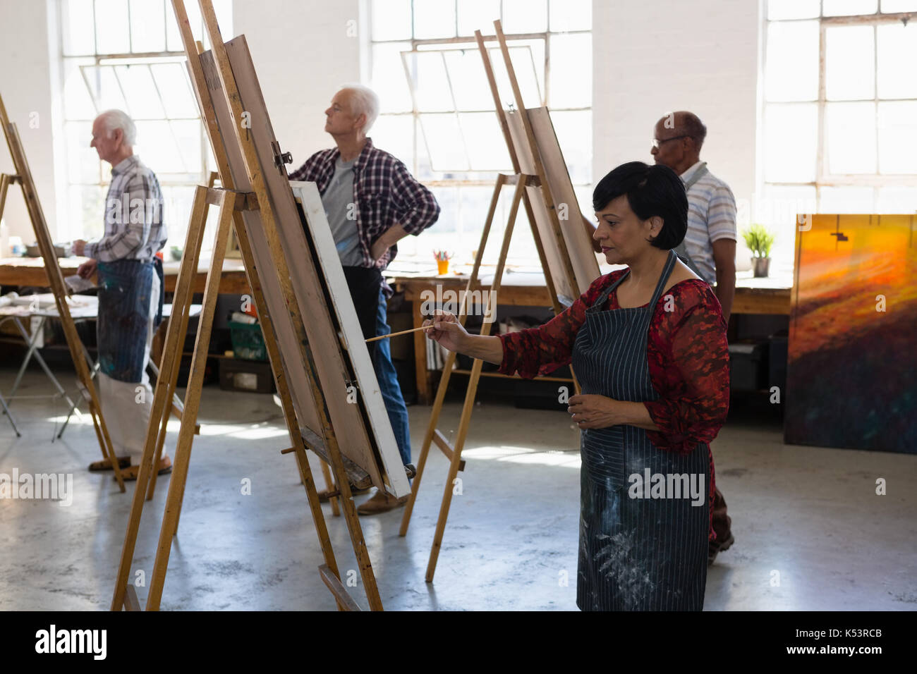 Senior male and female artists painting on easel while standing in art ...