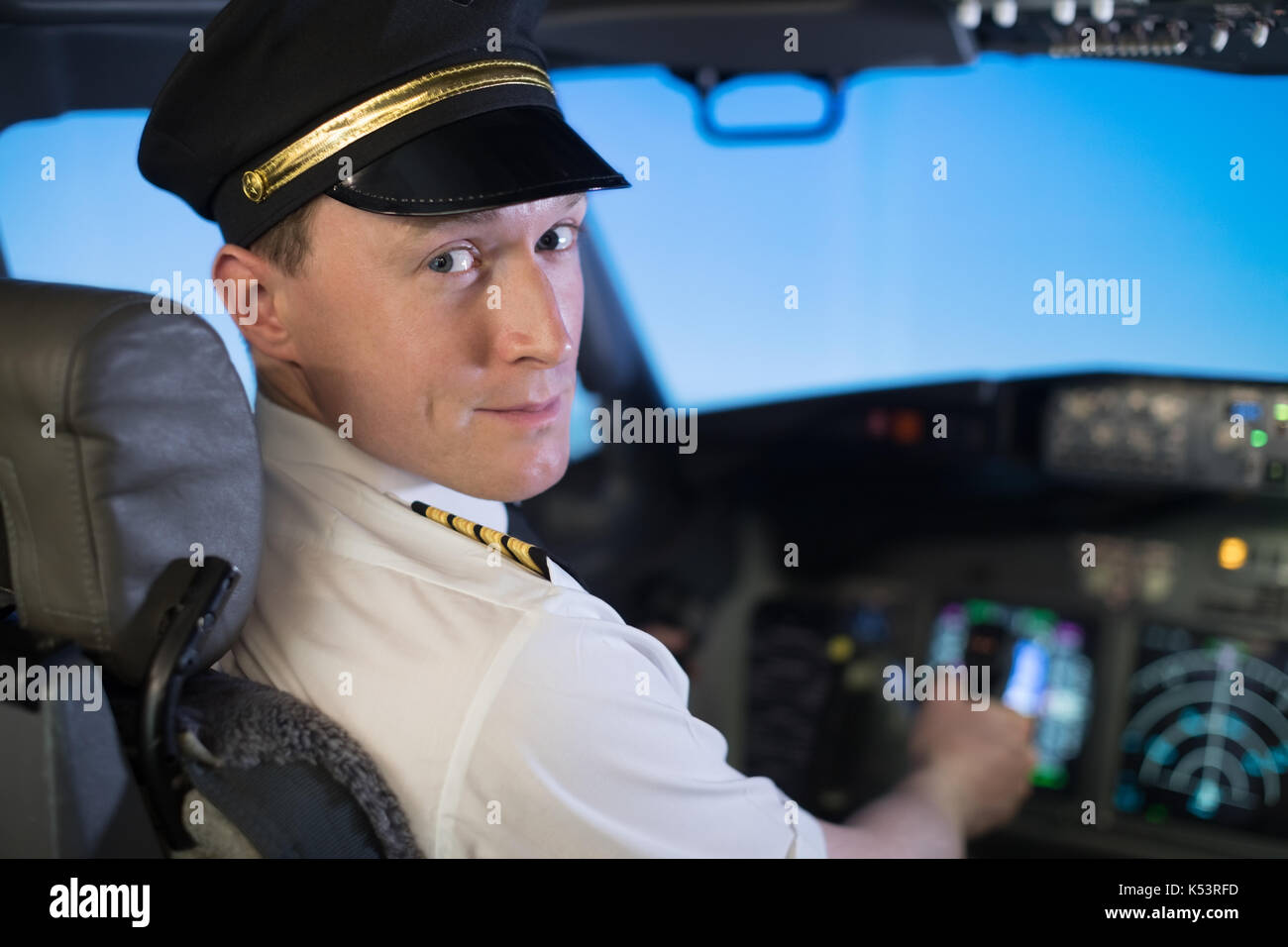 Close up portrait of confident young male pilot flying airplane while sitting on seat in cockpit ...