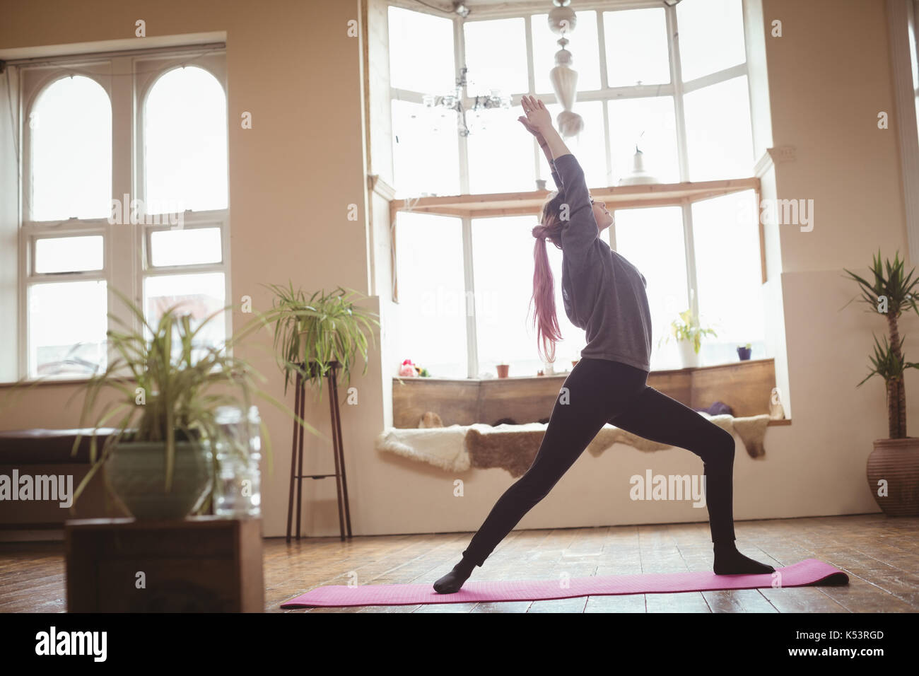Full length of young woman with arms raised doing yoga on exercise mat ...