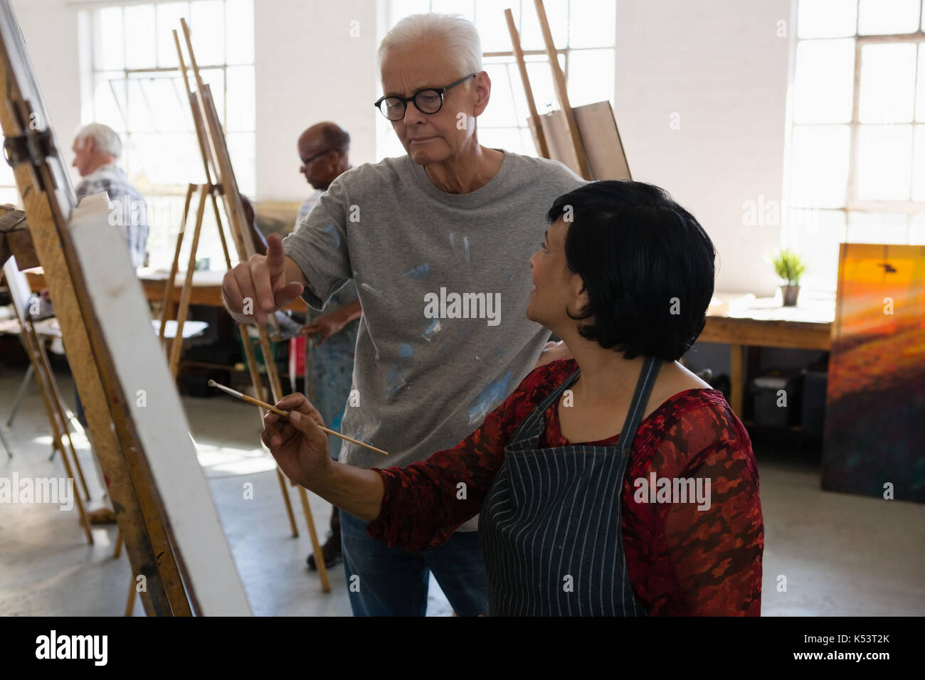 Man assisting female artist while painting in art class Stock Photo - Alamy
