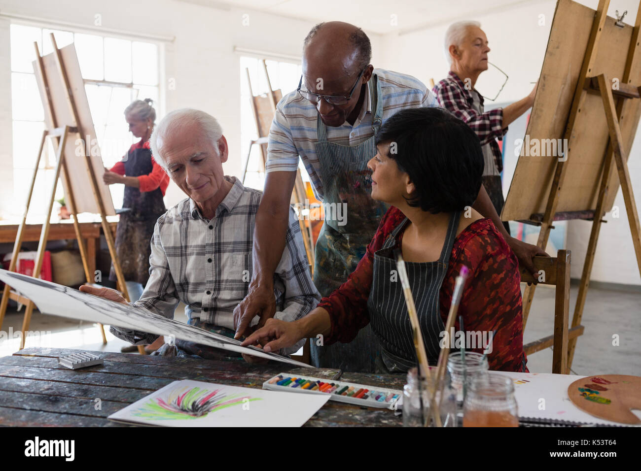 Senior friends assisting man while painting in art class Stock Photo ...