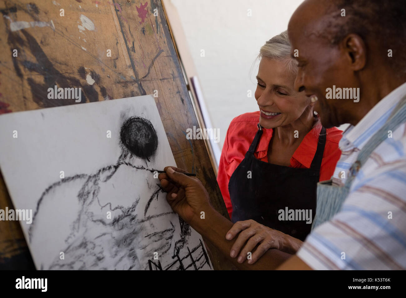 Senior woman assisting man while painting on paper in art class Stock ...