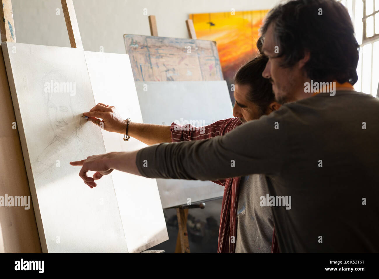 Man assisting friend while painting on canvas in art class Stock Photo ...