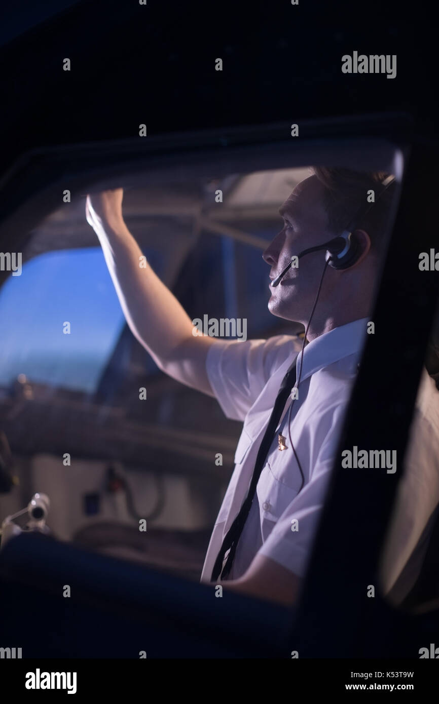 Side view of male pilot switching control in airplane cockpit seen from ...