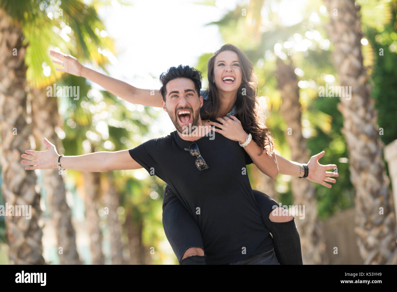 Portrait of man giving his girlfriend a piggy back ride with spread arms Stock Photo - Alamy