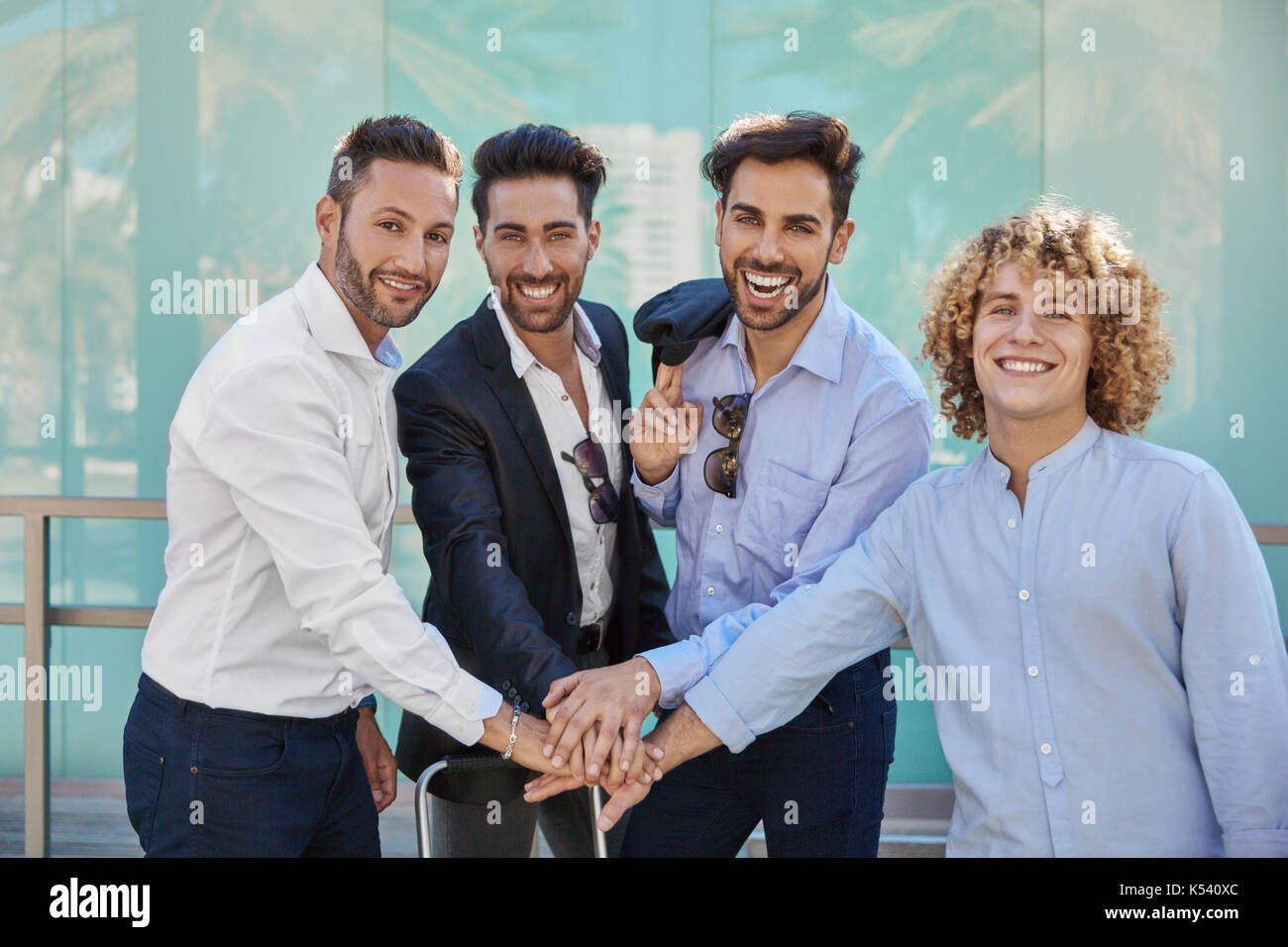 Front portrait of four laughing businessmen holding hands together ...