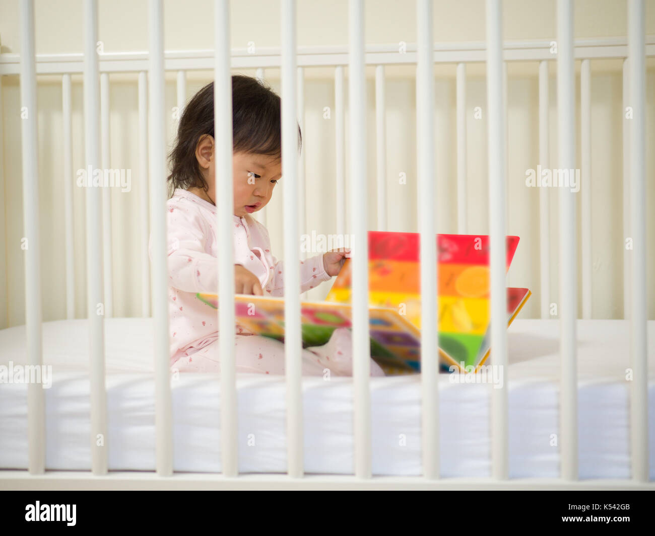 Baby girl reading book in cot bed Stock Photo - Alamy