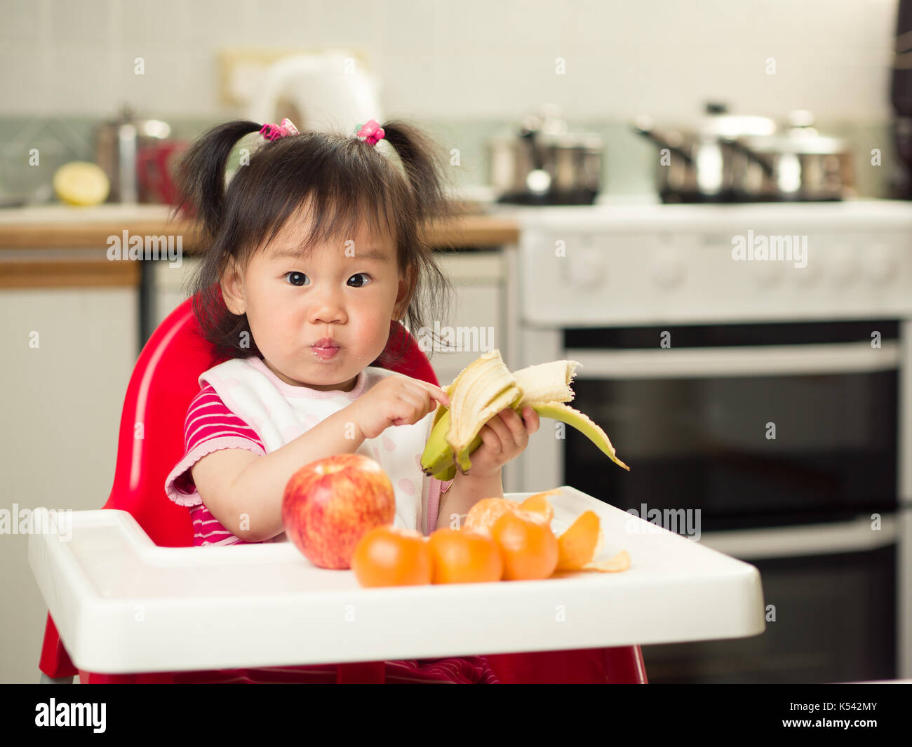 baby girl eating fruit at home Stock Photo - Alamy