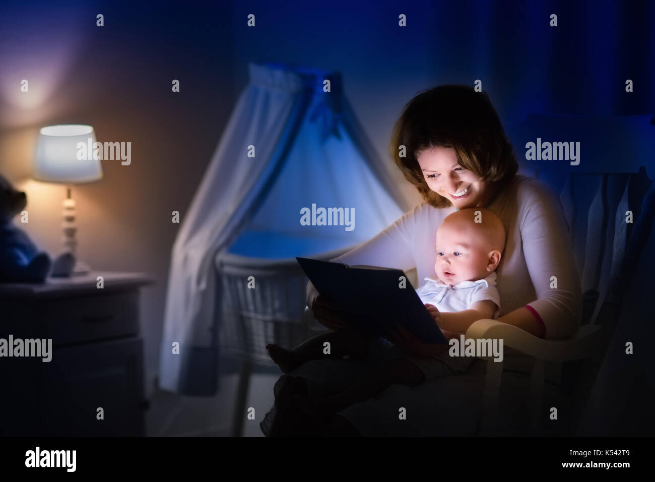 Mother and baby reading a book in dark bedroom. Mom and child read ...