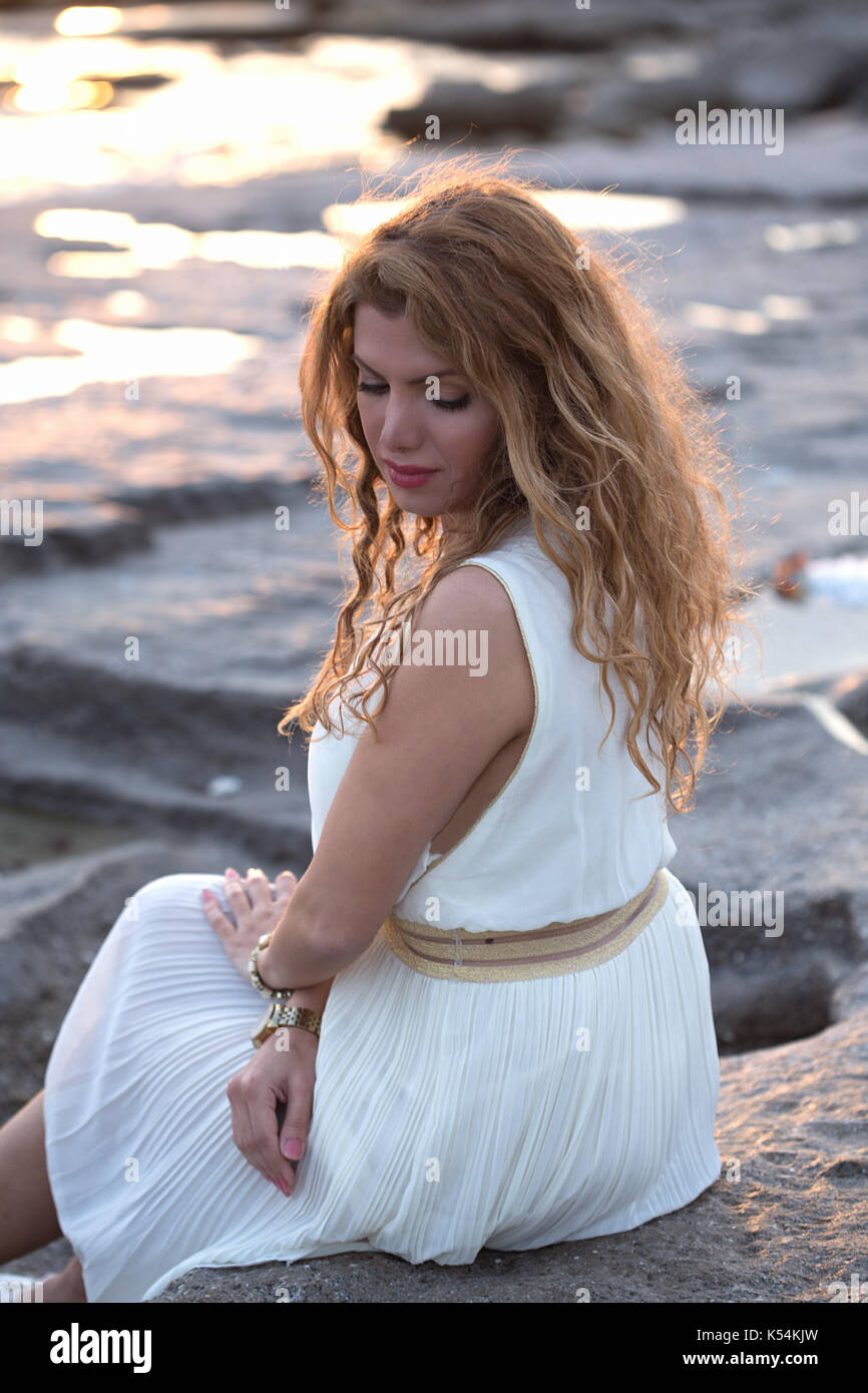 Beautiful lady in ivory dress sitting on rocks and thinking Stock Photo ...