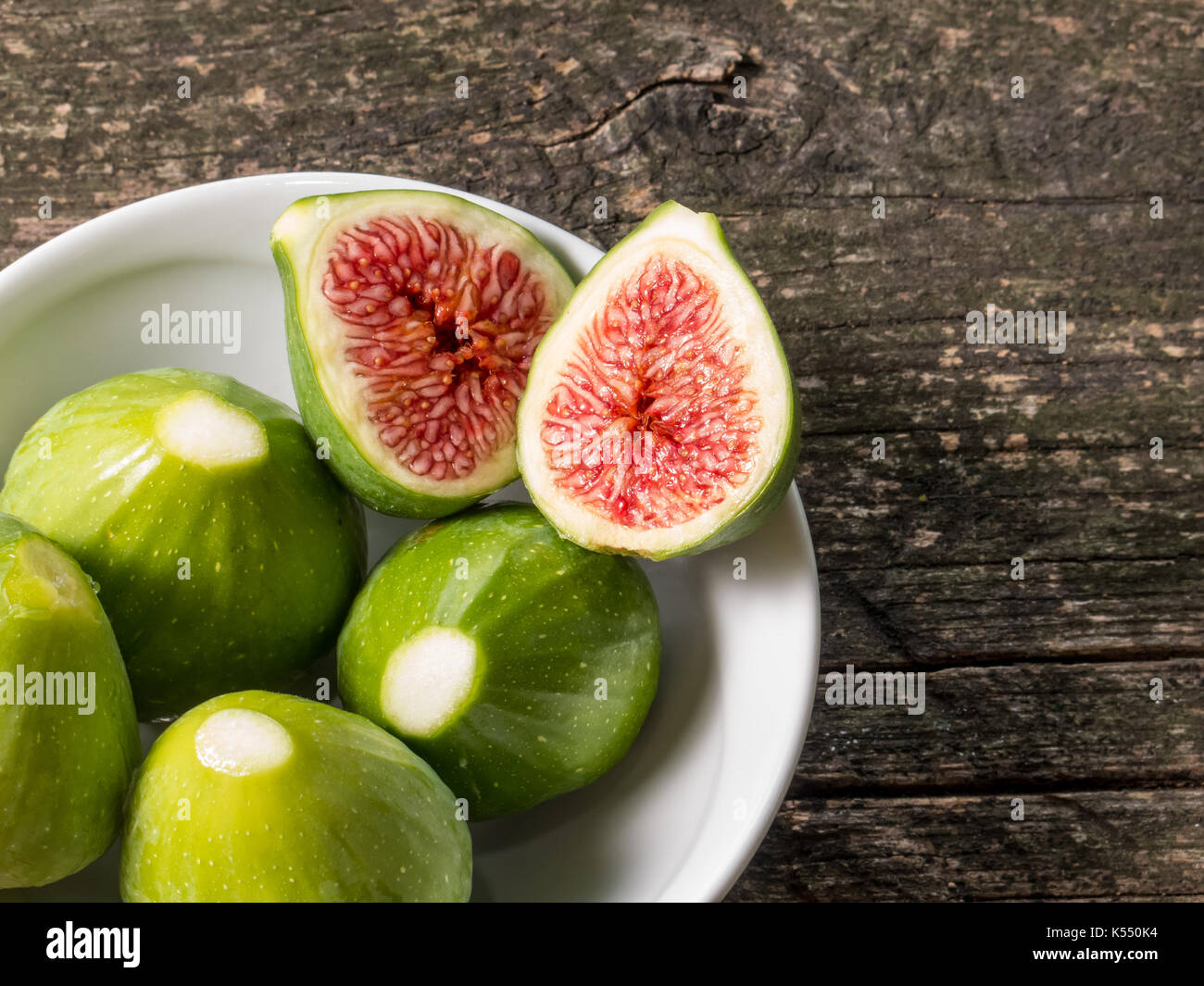 A white porcelain bowl with some ripe figs inside and one fig cut in ...