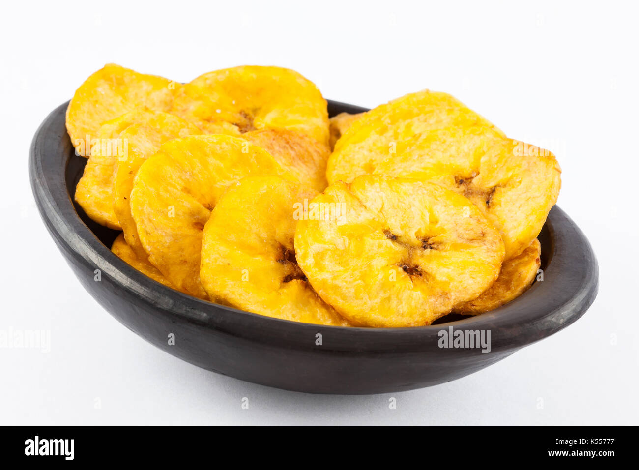 Plantain fried coins in a traditional black clay bowl isolated on white ...