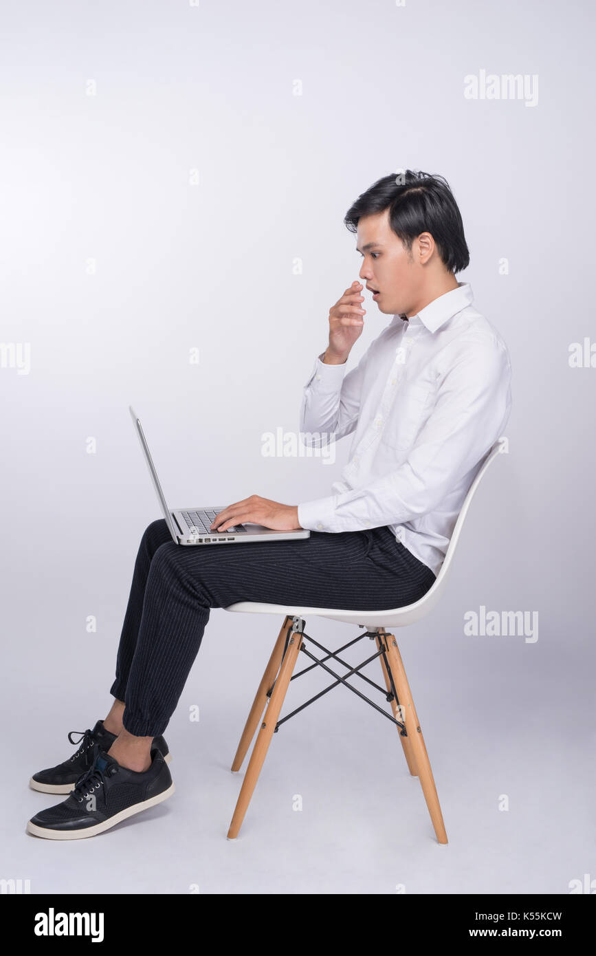 Smart casual asian man seated on chair, using laptop in studio ...