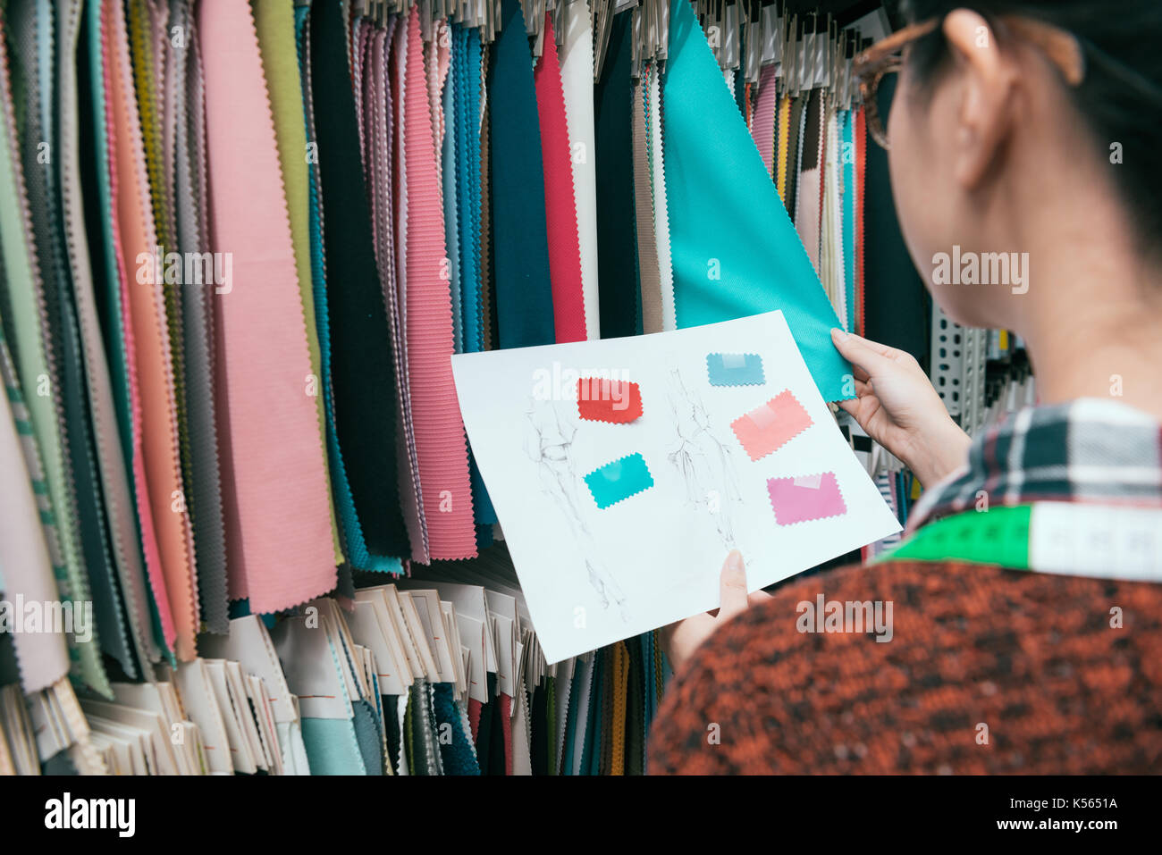 back view photo of female clothing maker using design paper choosing ...