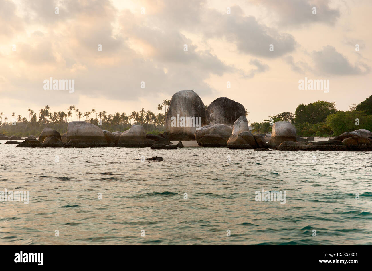 Natural rock formation in sea and on white sand beach with palm trees ...