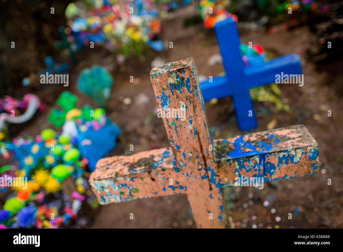 A grave cross, with flaked off blue paint, is seen among colorfully ...