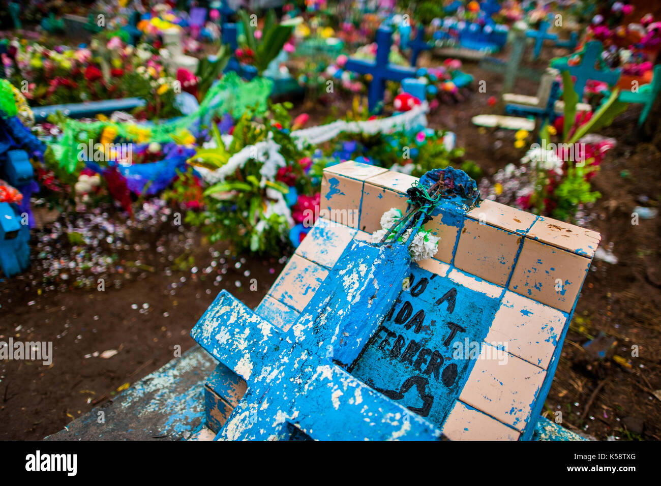 A broken tomb cross, with flaked off paint, is seen among colorfully ...