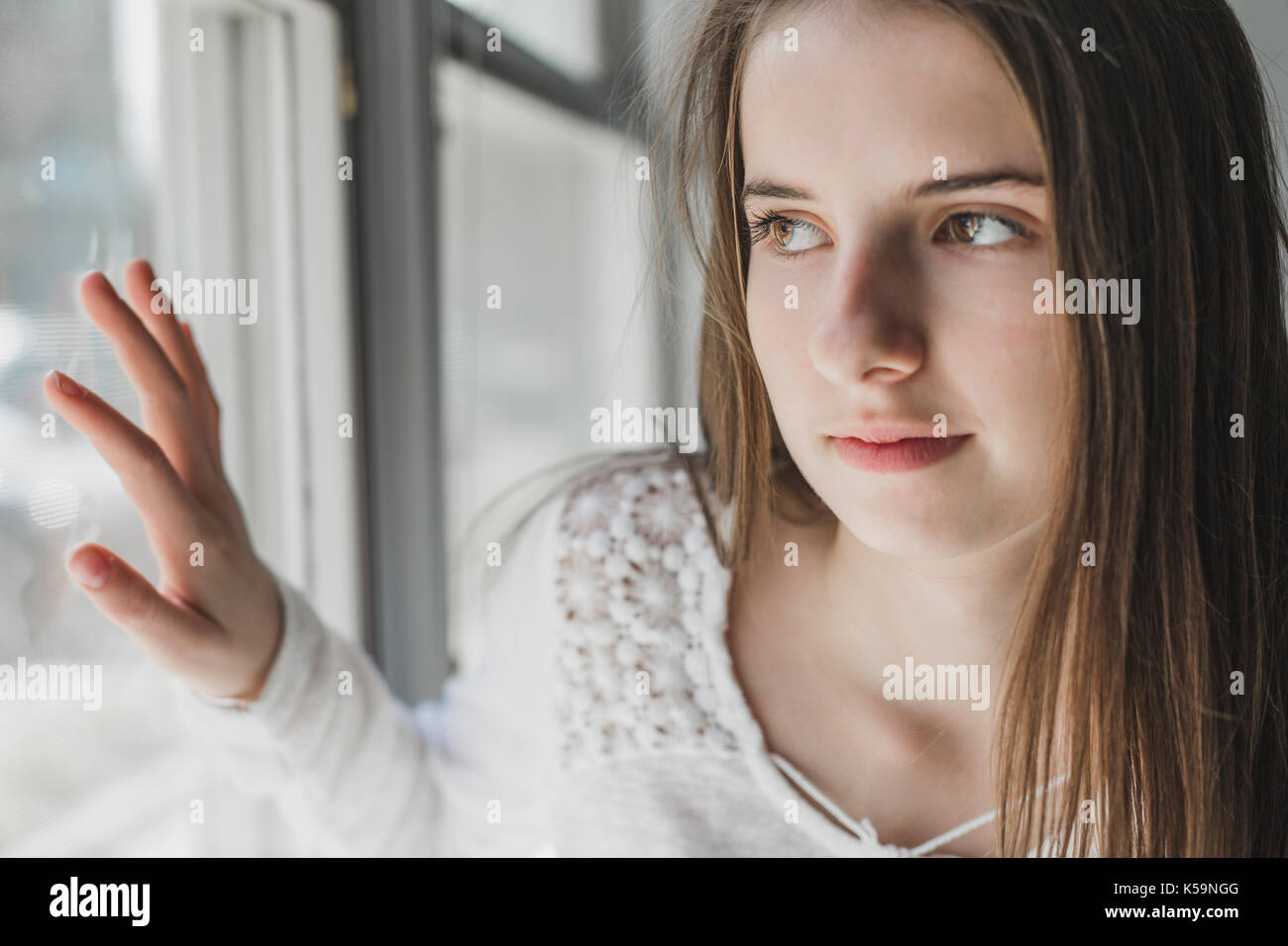 Beautiful young woman in front of a window looking outside Stock Photo ...